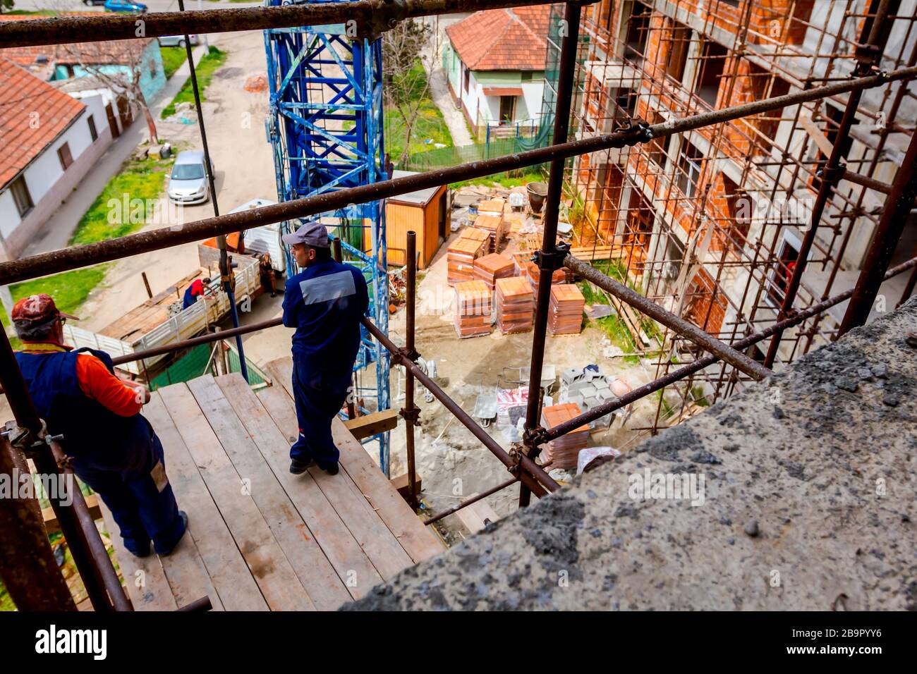 Riggers are standing on scaffold with wooden platform high up on ...
