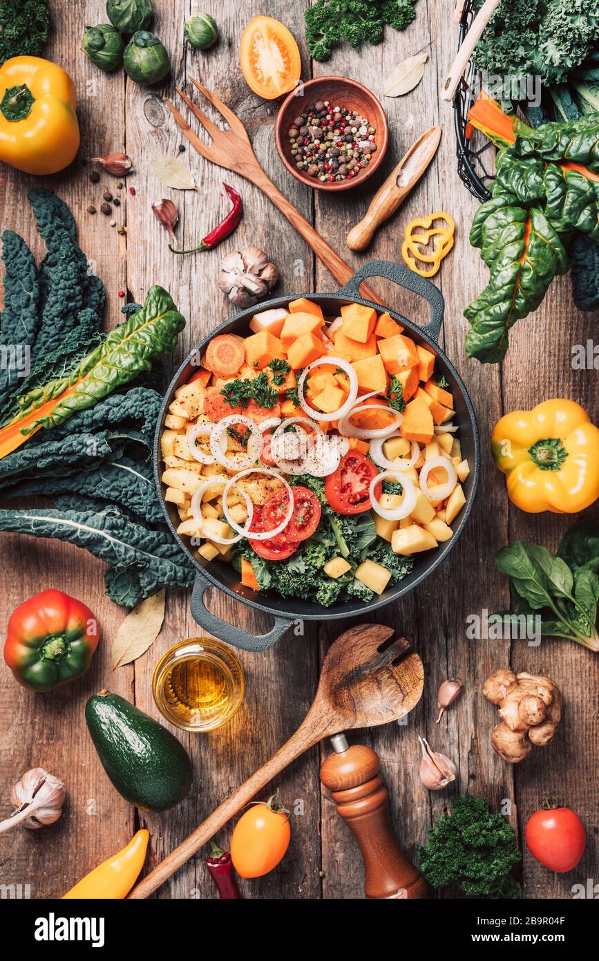 Pot with sliced colorful vegetables and cooking utensils on rustic ...