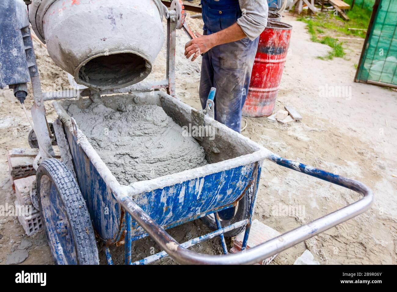 Worker is pouring concrete from cement mixer into wheelbarrow Stock ...