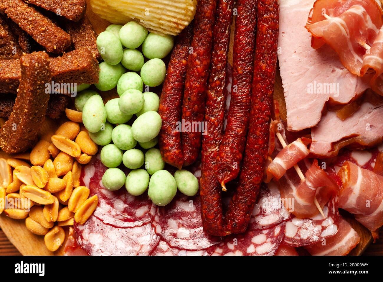 Assorted beer snacks on a wooden table with copy space. Sausage, ham, bacon. Salty snack chips ...