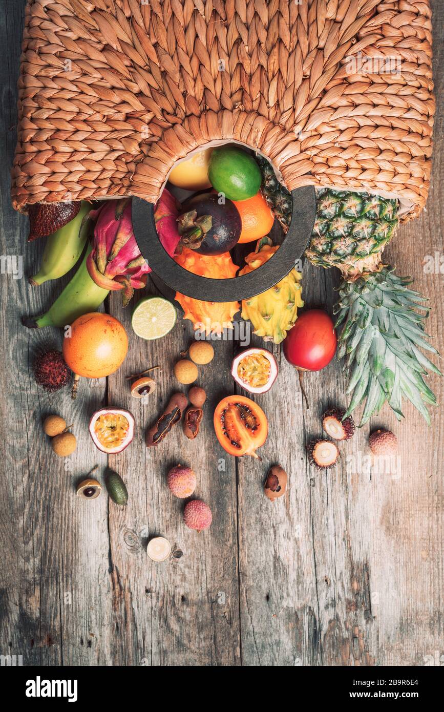 Exotic fruits in straw summer bag on wooden background. Top view. Copy ...