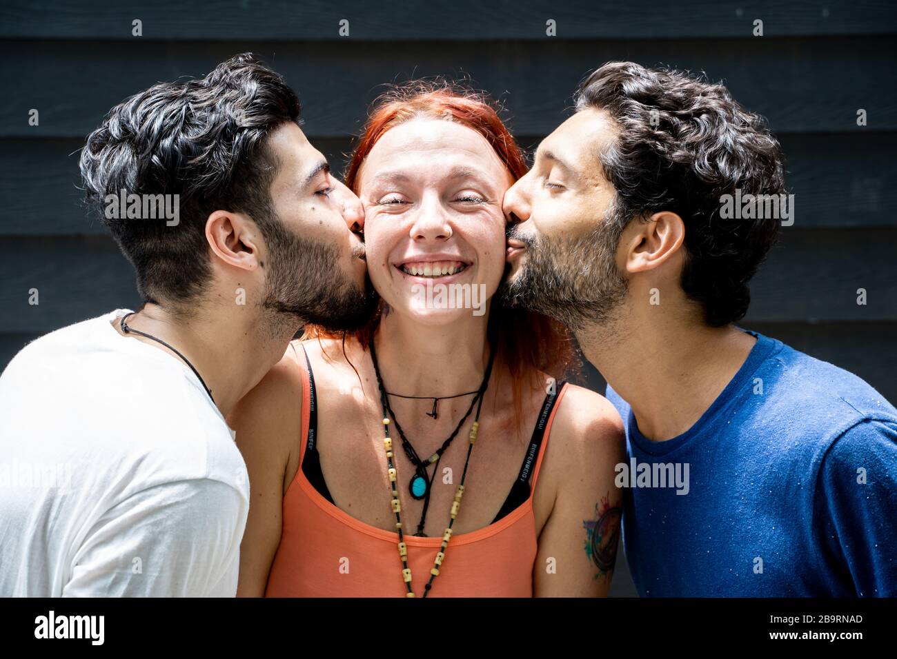 Two young boys of different ethnicities kissing on the cheek of a girl ...