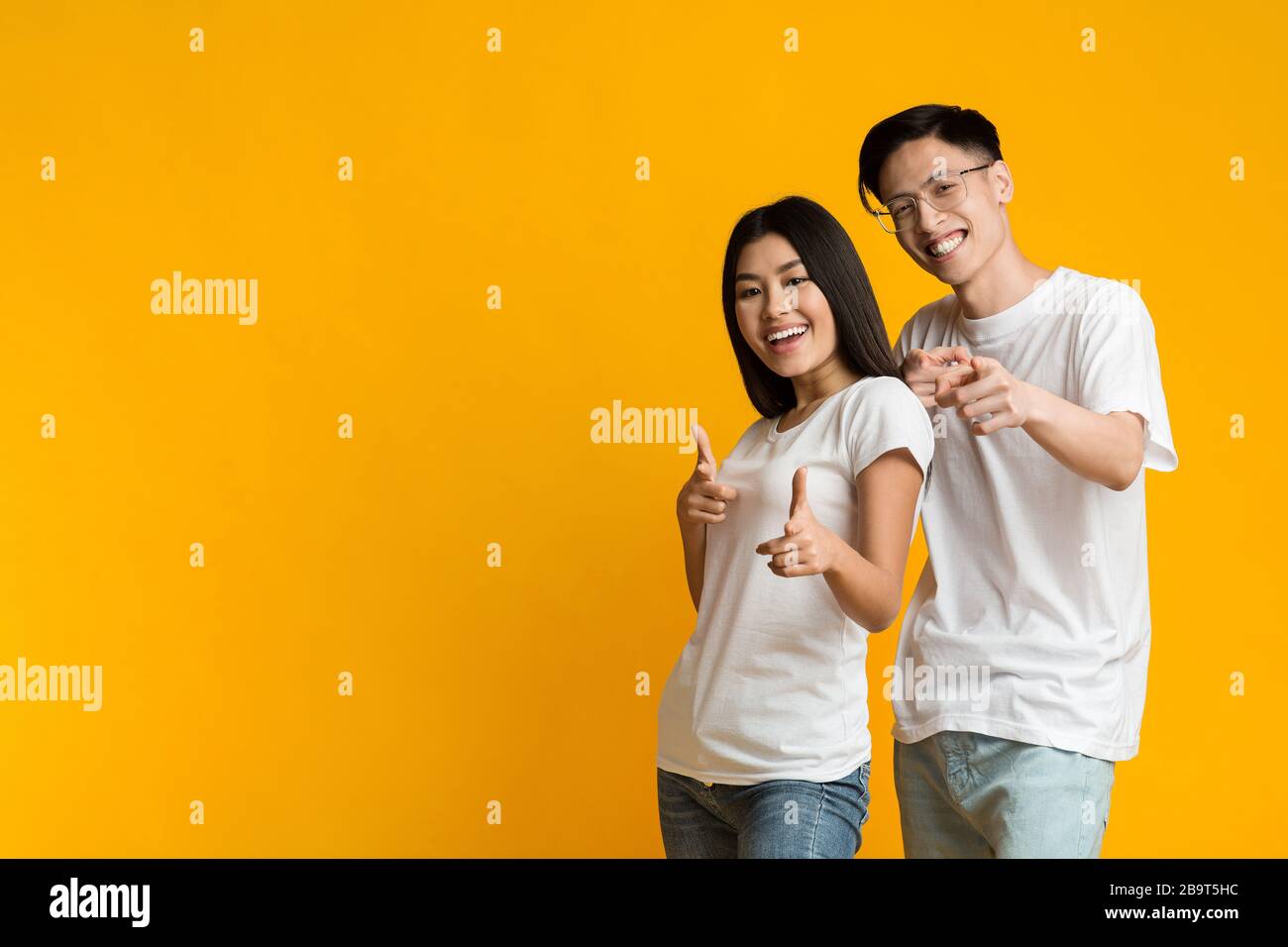 Friendly asian couple indicating at camera over yellow background Stock ...