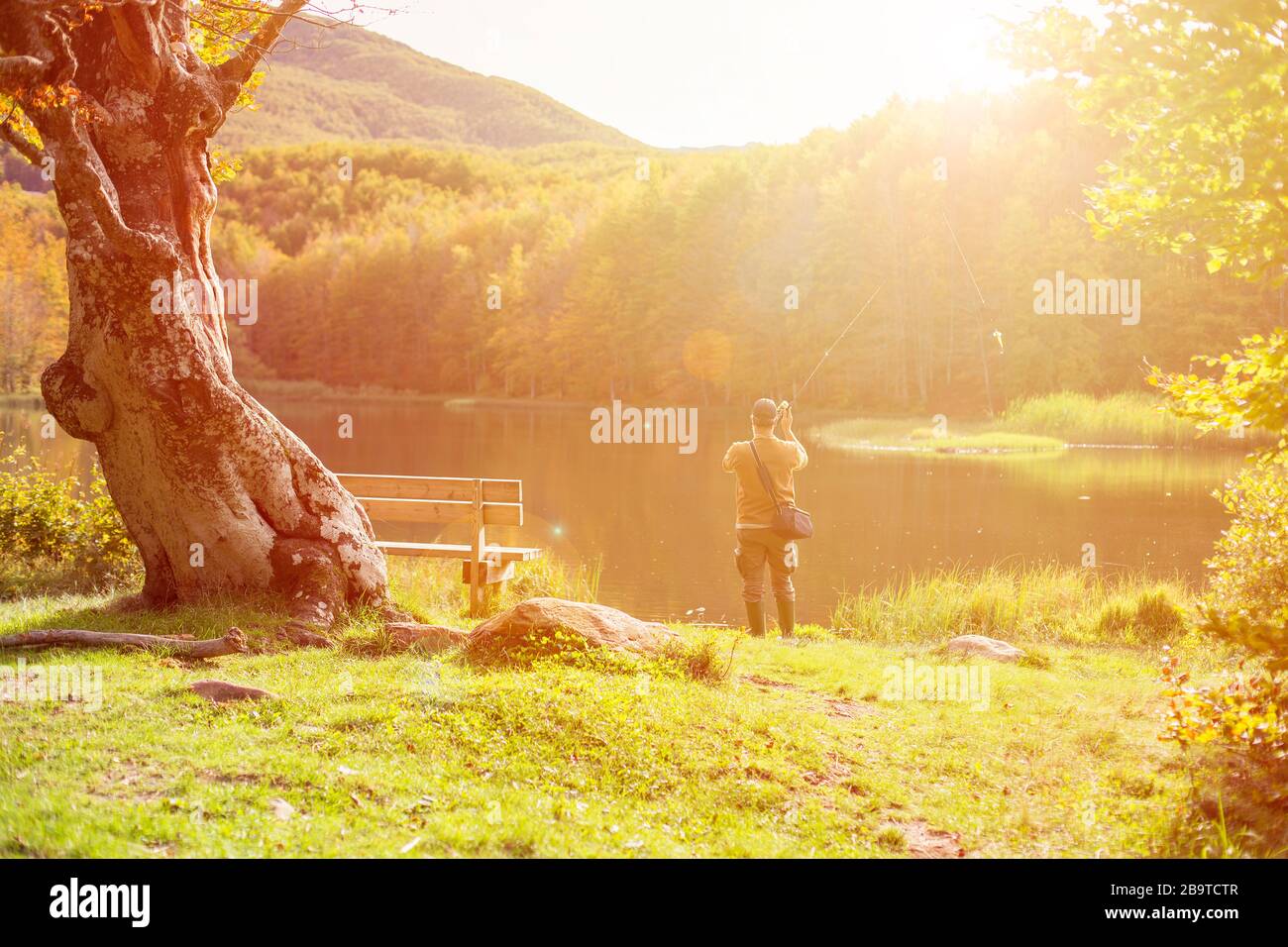 fisherman while casting line to fish in a mountain lake surrounded by ...