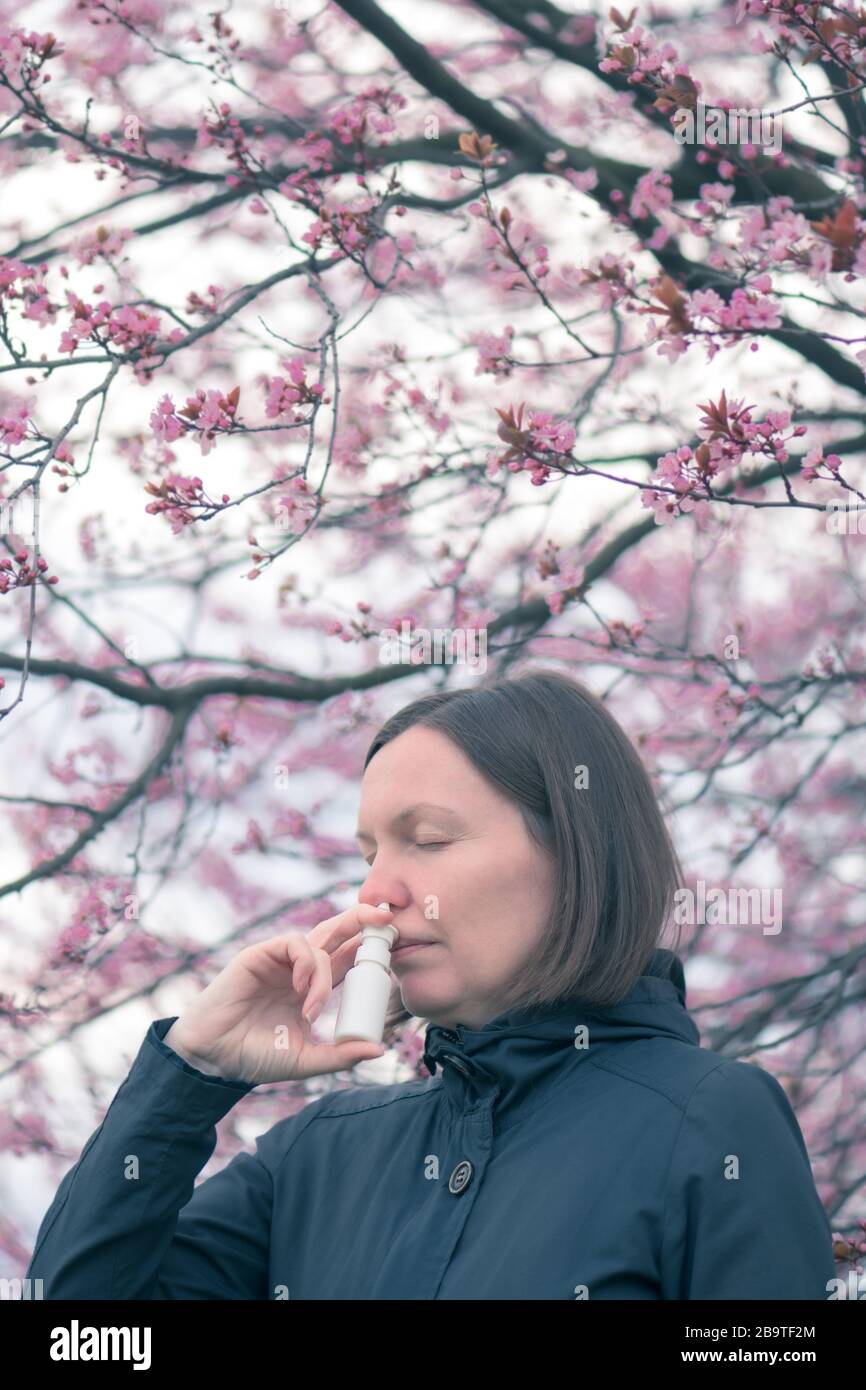 Woman using nasal spray outdoors for tree pollen allergy treatment ...