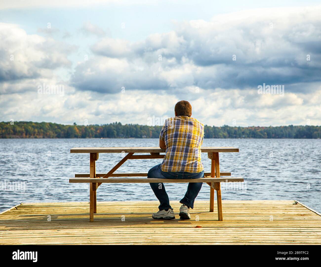 Man sitting on a bench in front of a lake Stock Photo - Alamy