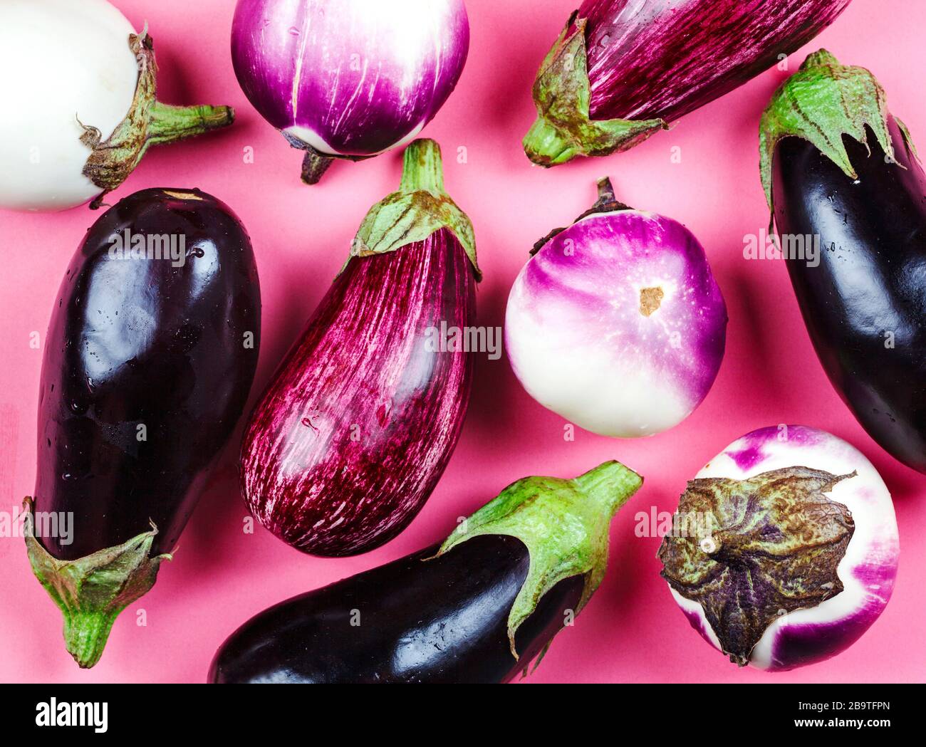 Fresh raw eggplants of different color and variety on a pink background ...