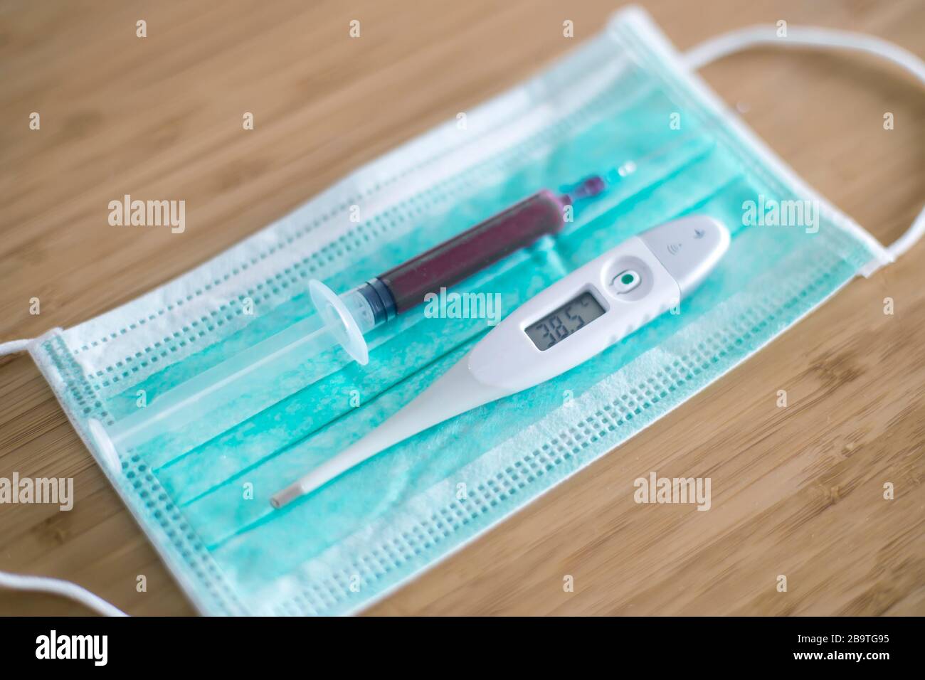 Surgical ear-loop mask, injection syringe and thermometer on the table ...