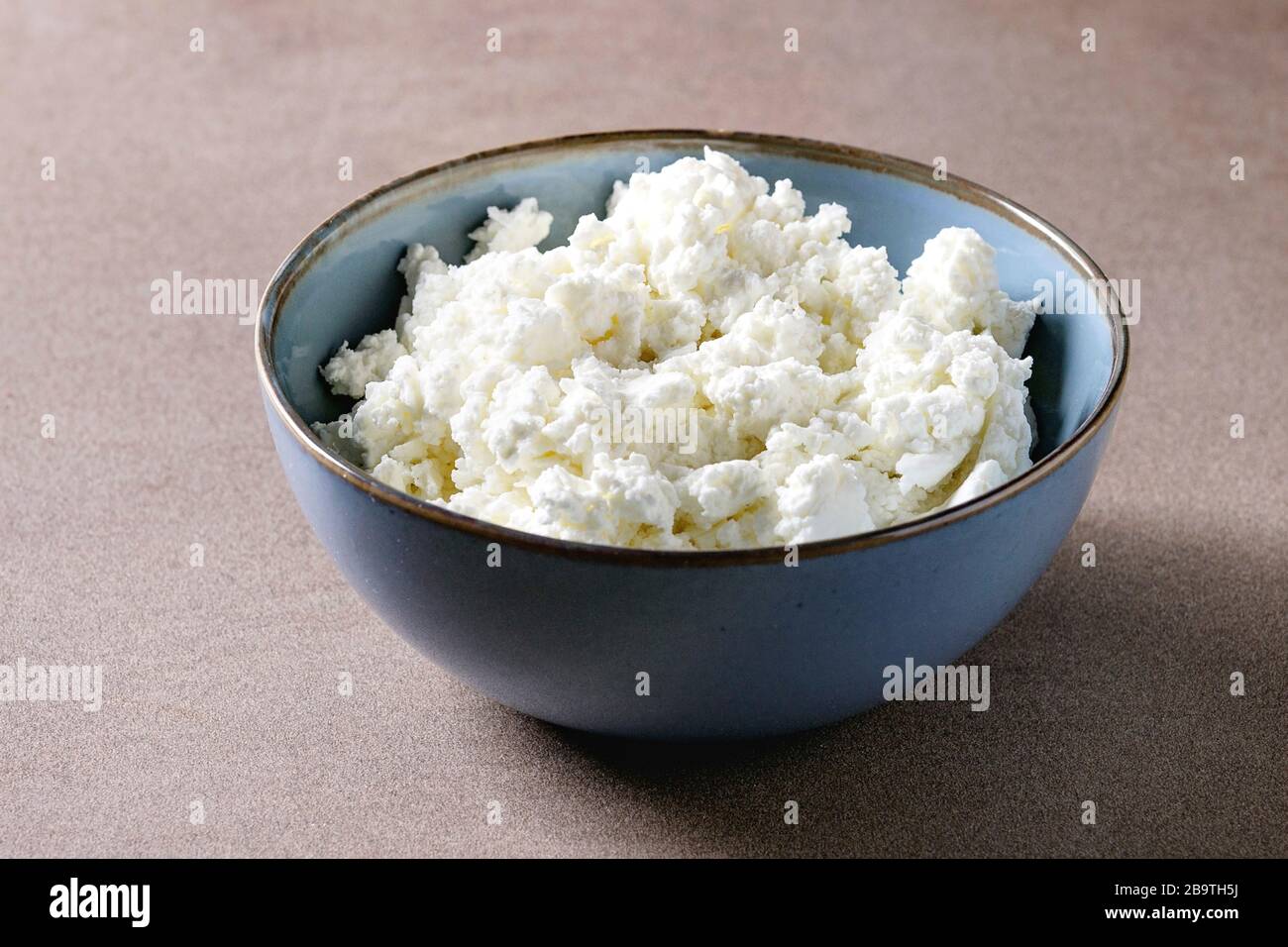 Fresh organic cottage cheese in blue ceramic bowl on brown texture ...