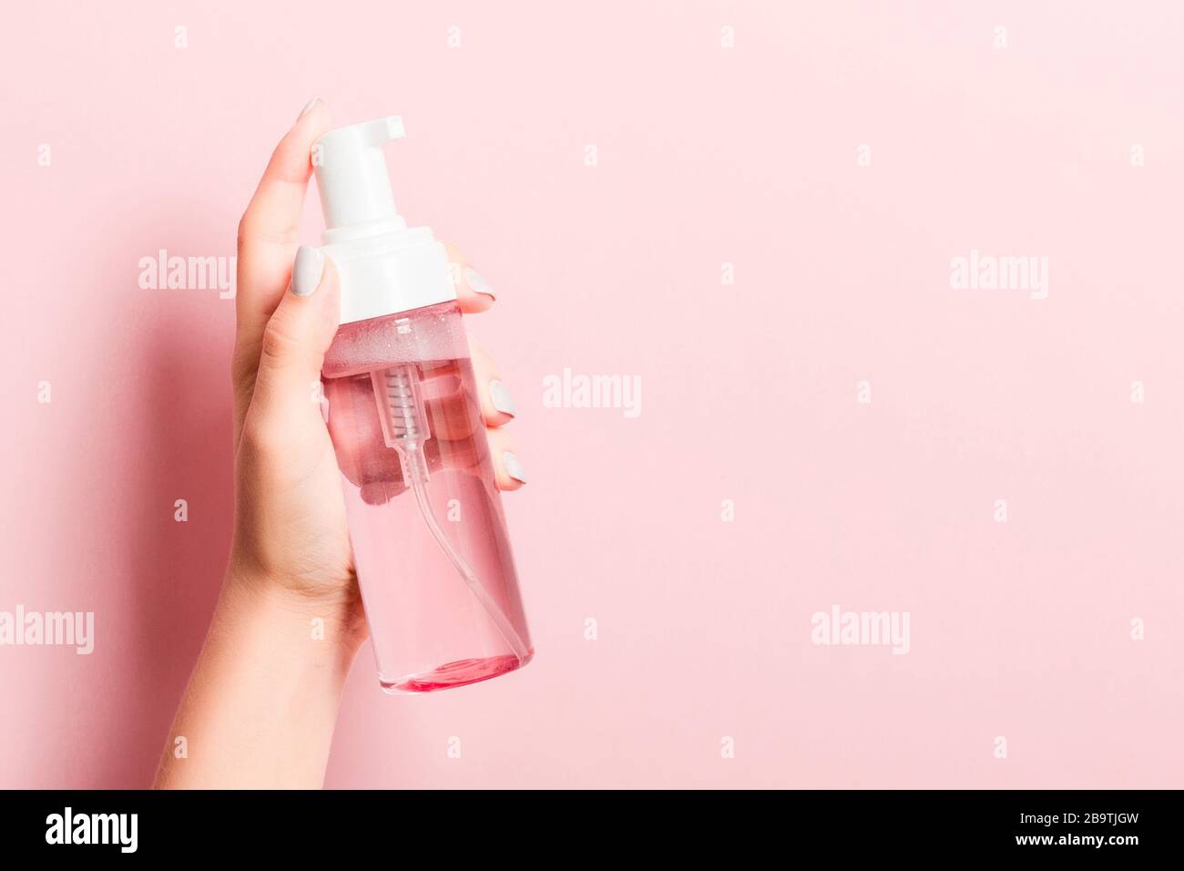 Woman's hand is holding a cosmetics spray at pink background with copy ...