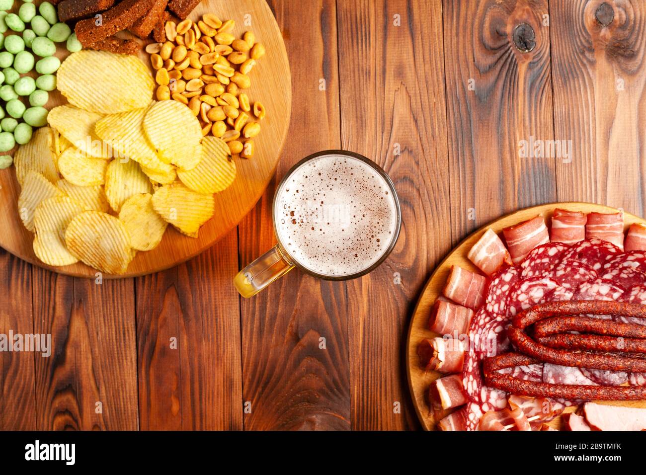 Mug of beer and assortment of snacks on a wooden table. Sausage, salami ...
