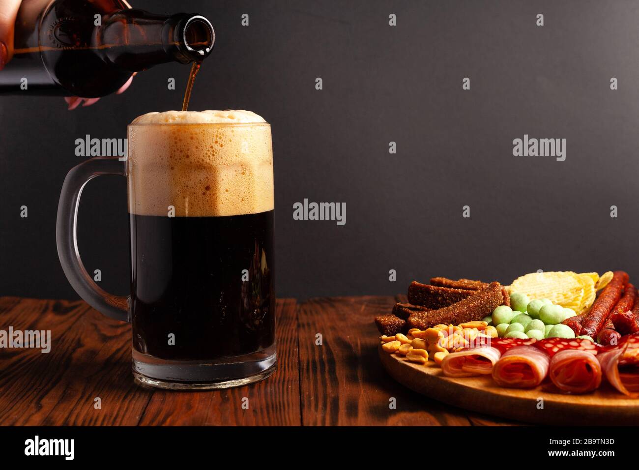 Mug of beer and assortment of snacks on a wooden table. Sausage, salami ...