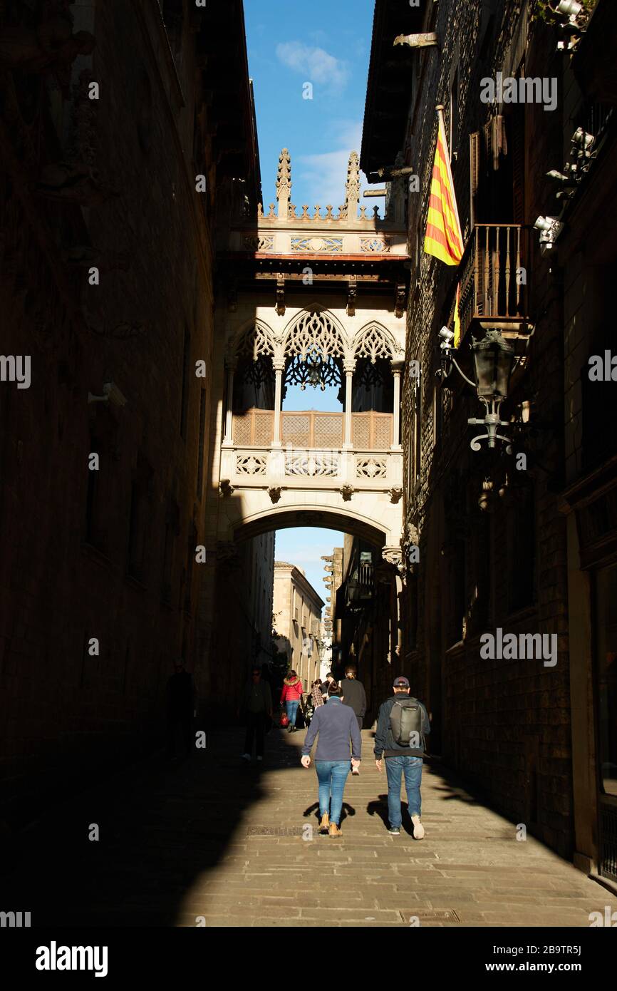 People walking under the Pont del Bisbe at sunrise in the Bari Gotic in ...