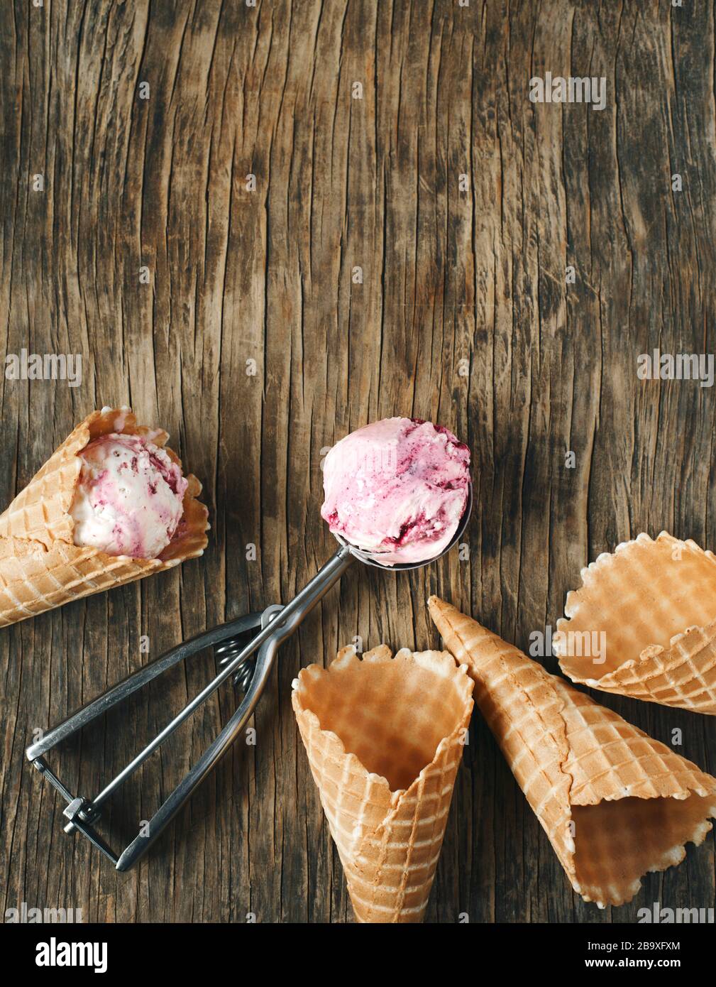 Raspberry vanilla ice cream scoop in a spoon with waffles cones on ...
