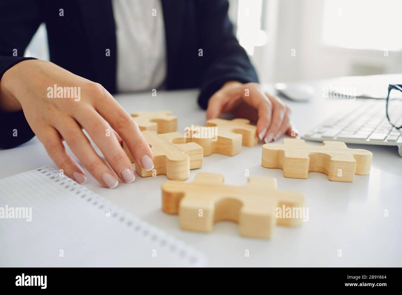 Faceless hands of a businesswoman with wooden puzzles on a white table ...