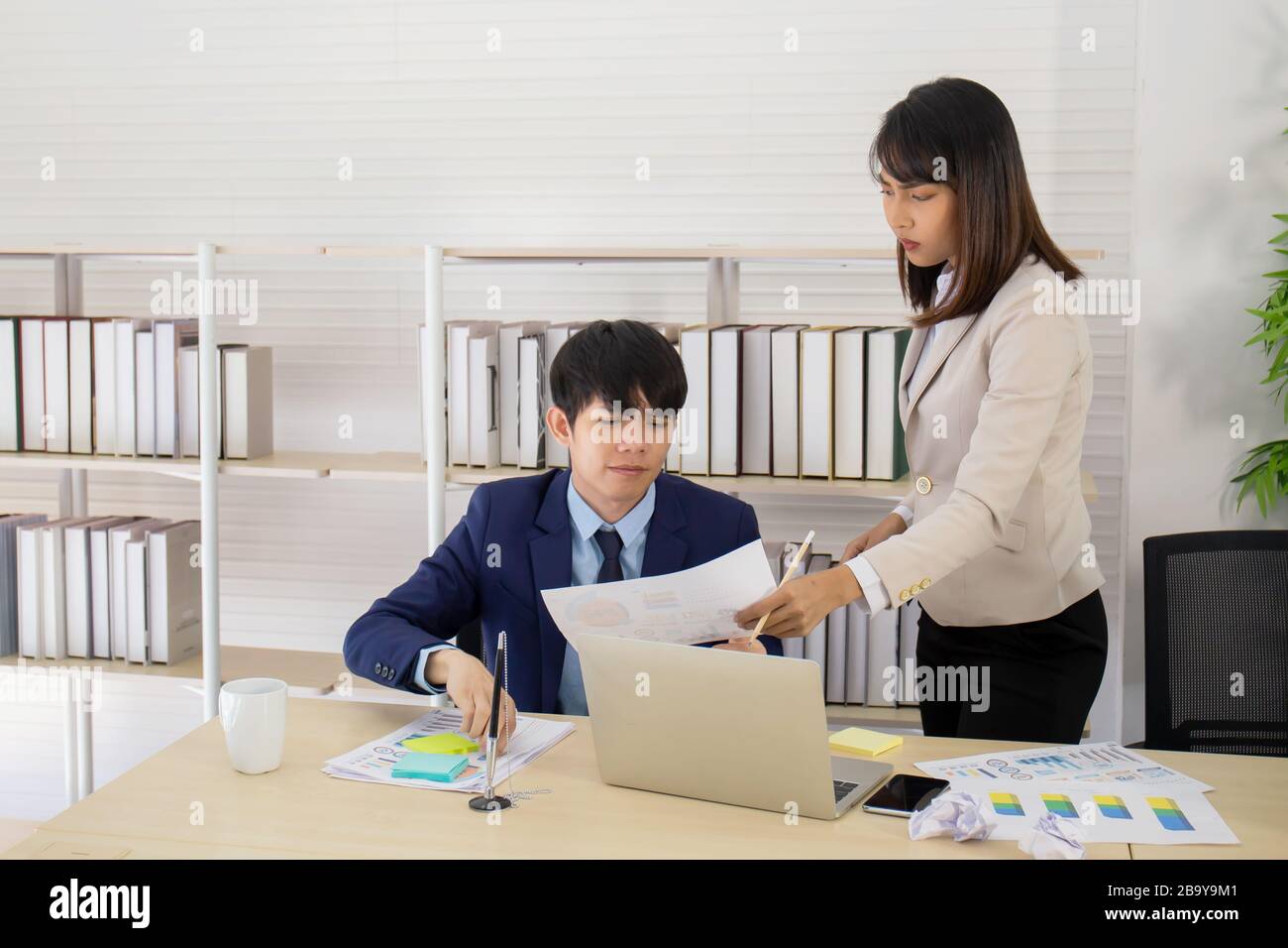 An Asian female supervisor stands with a young male employee on her ...
