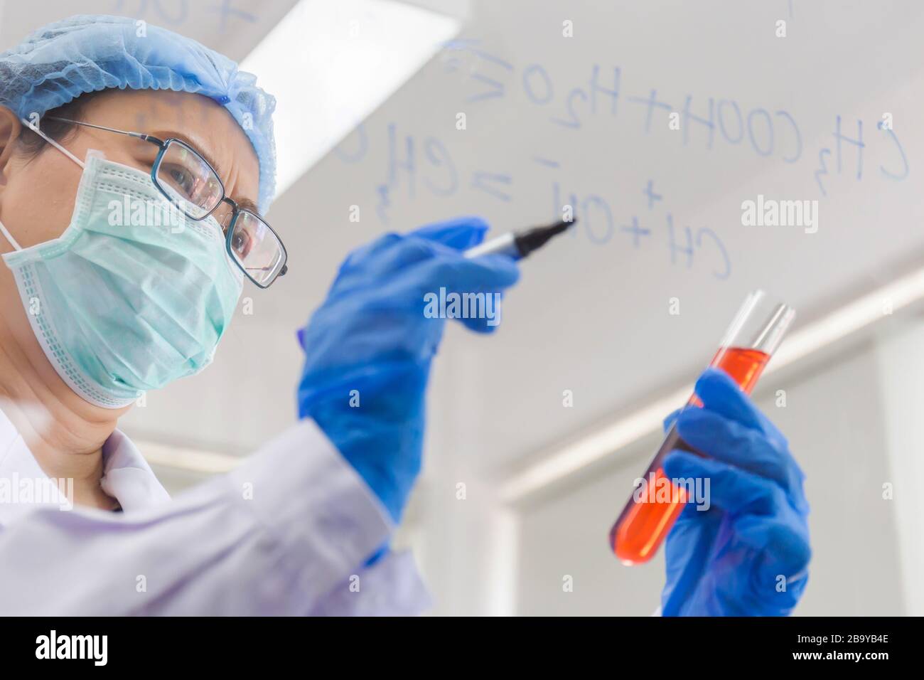 An Asian female scientist is writing down the formula for calculating ...
