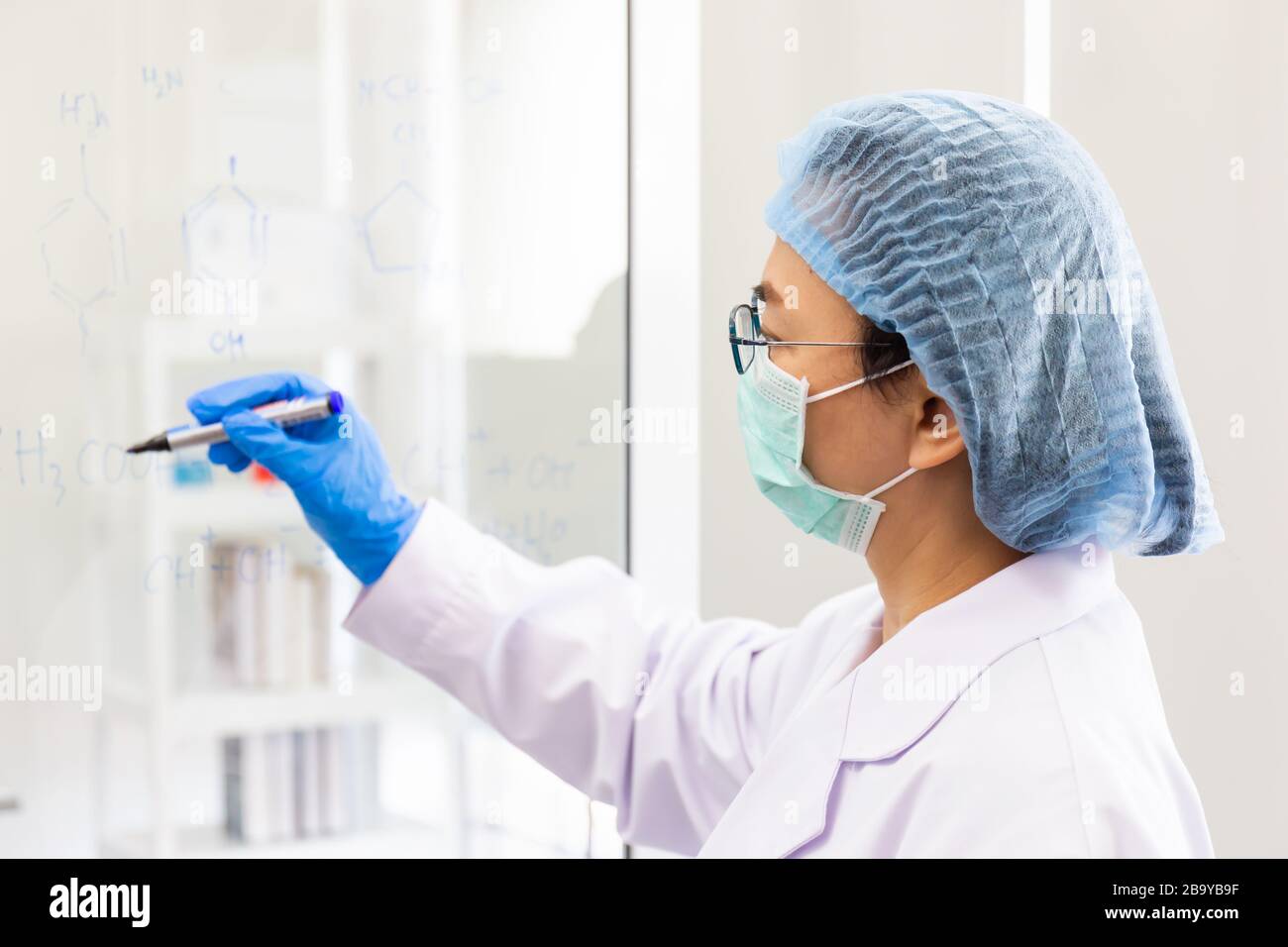 An Asian female scientist is writing down the formula for calculating ...