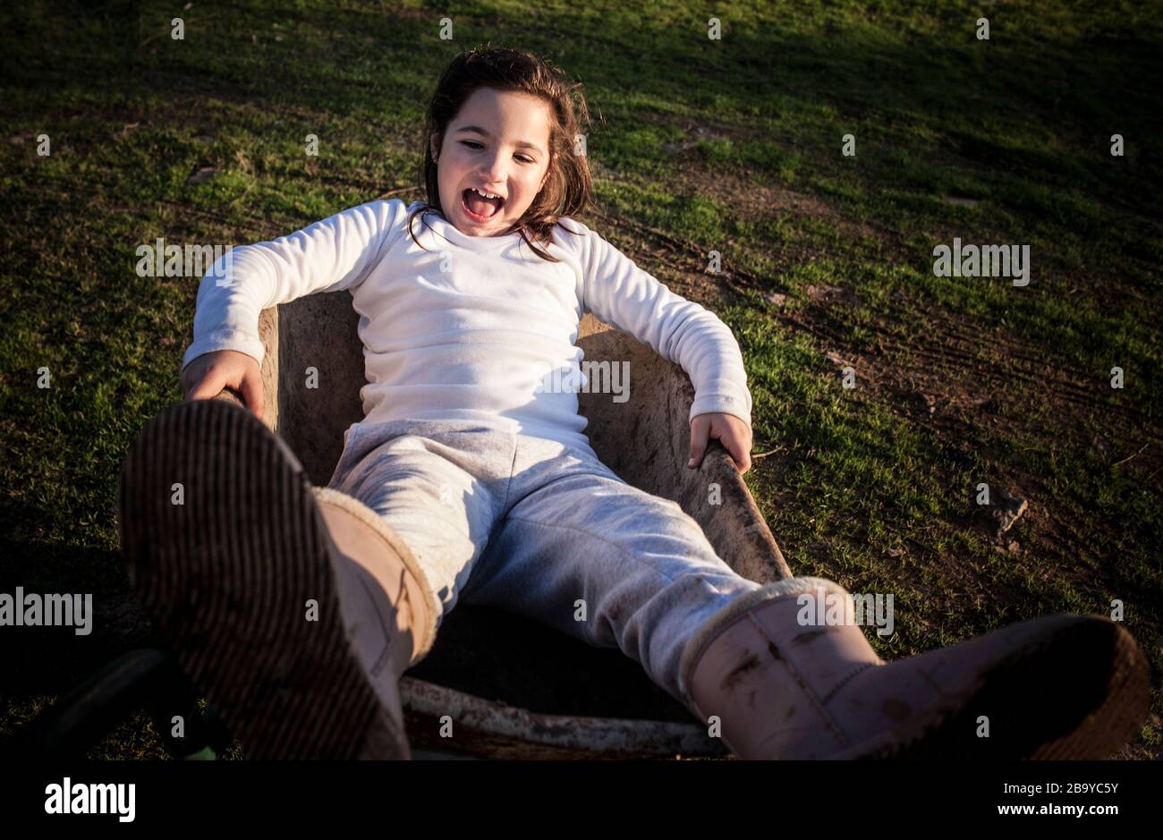 Little girl playing on old rusty farmer wheelbarrow. Funny country life ...