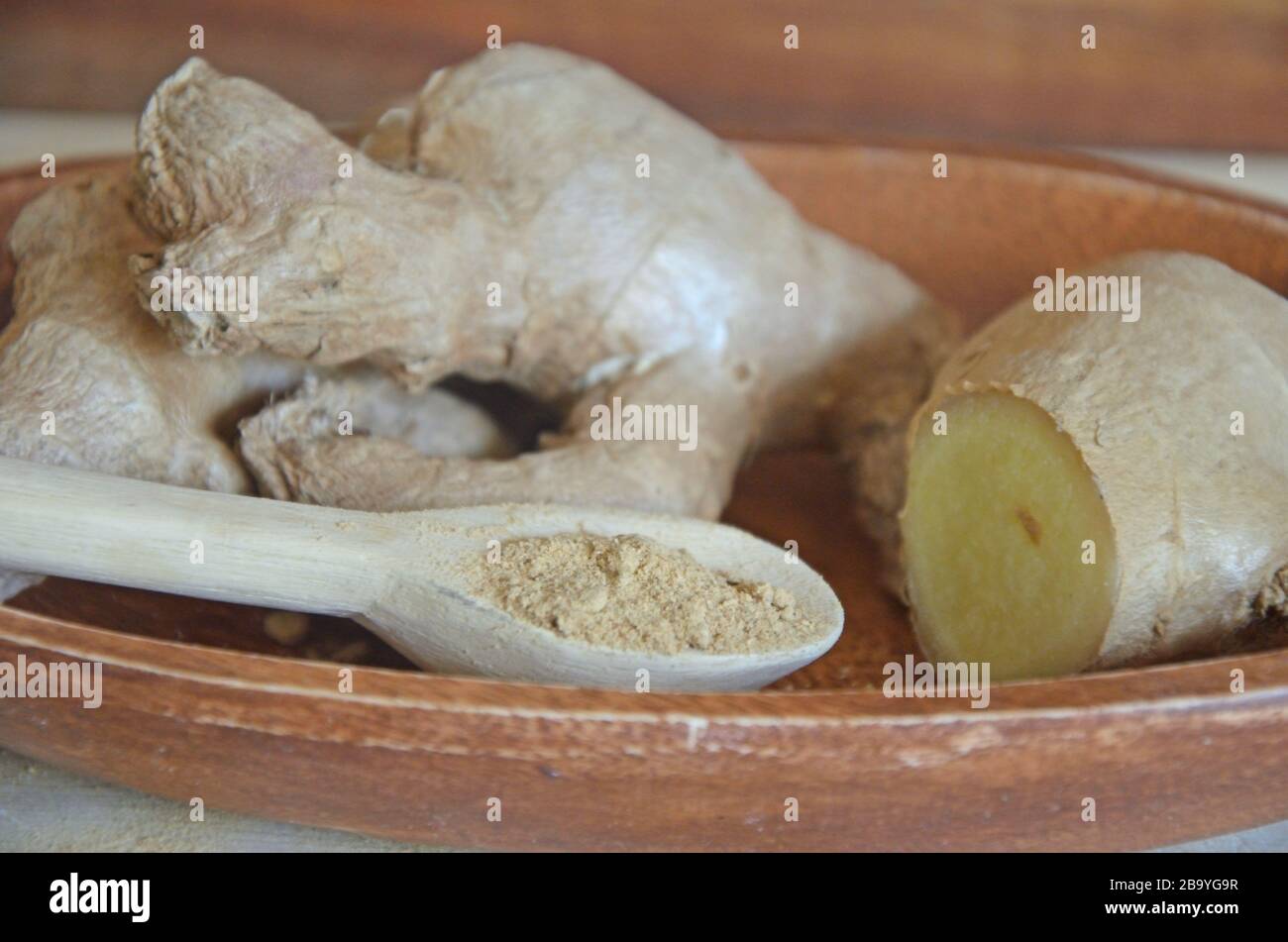 Fresh ginger root and slices, and crushed dried ginger in wooden bowl ...