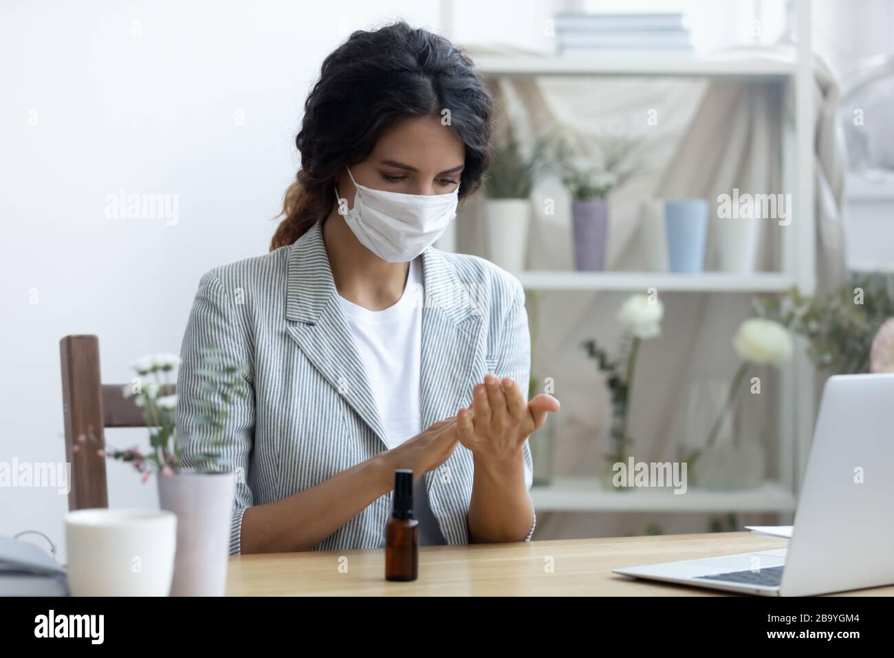 Female employee in mask use hand sanitizer at workplace Stock Photo - Alamy