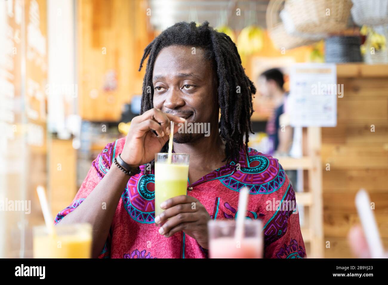 African young man with dreadlocks drinking a fruit juice in a cafeteria ...