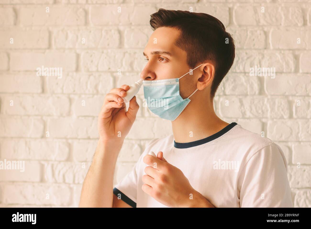 Portrait of young sick man using nasal drops for runny congested nose ...