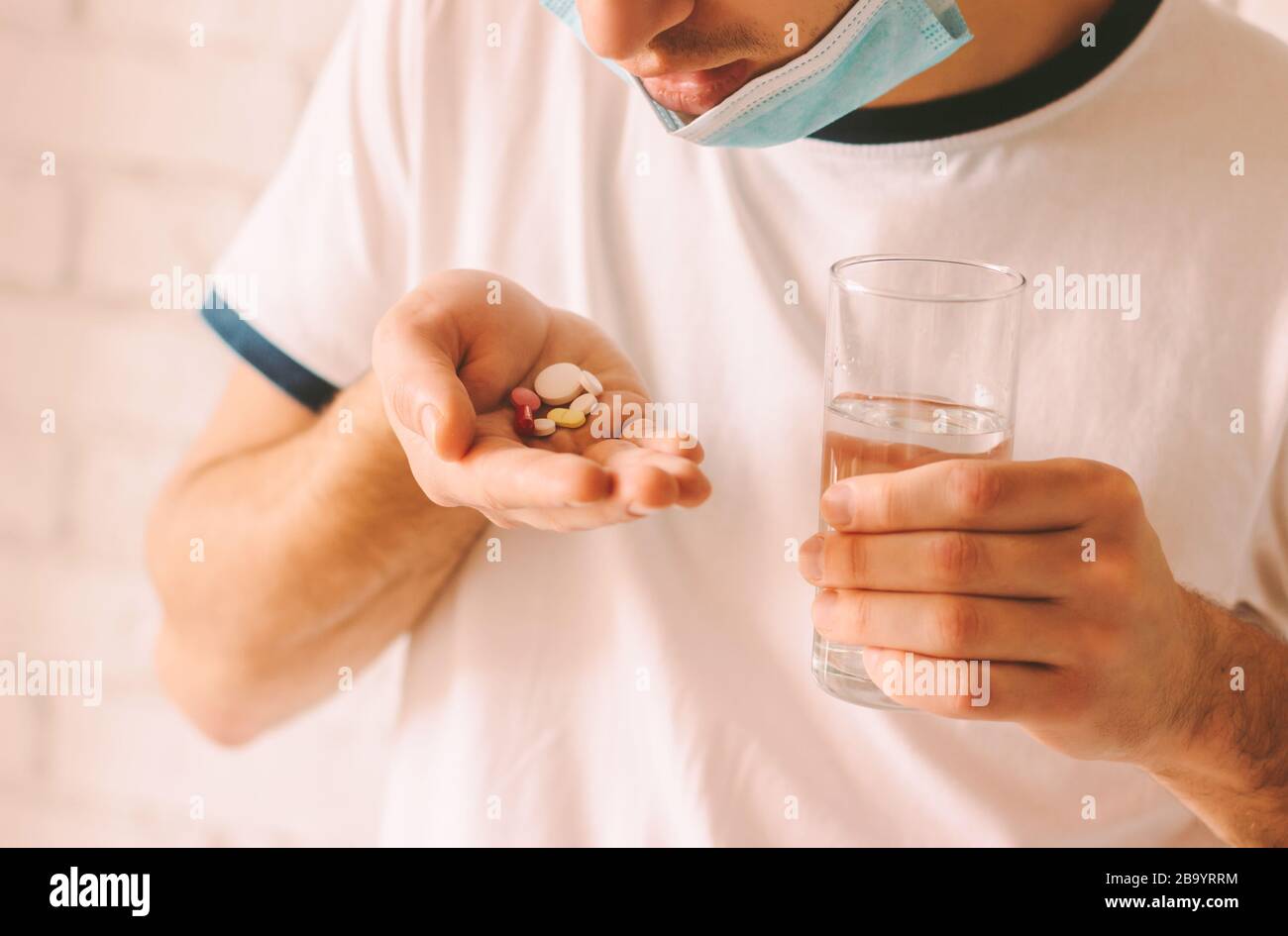 Closeup of young ill man taking different pills with glass of water in ...