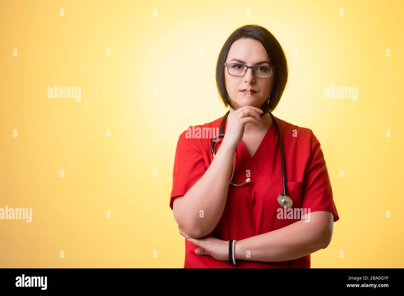 Portrait of beautiful woman doctor with stethoscope wearing red scrubs ...