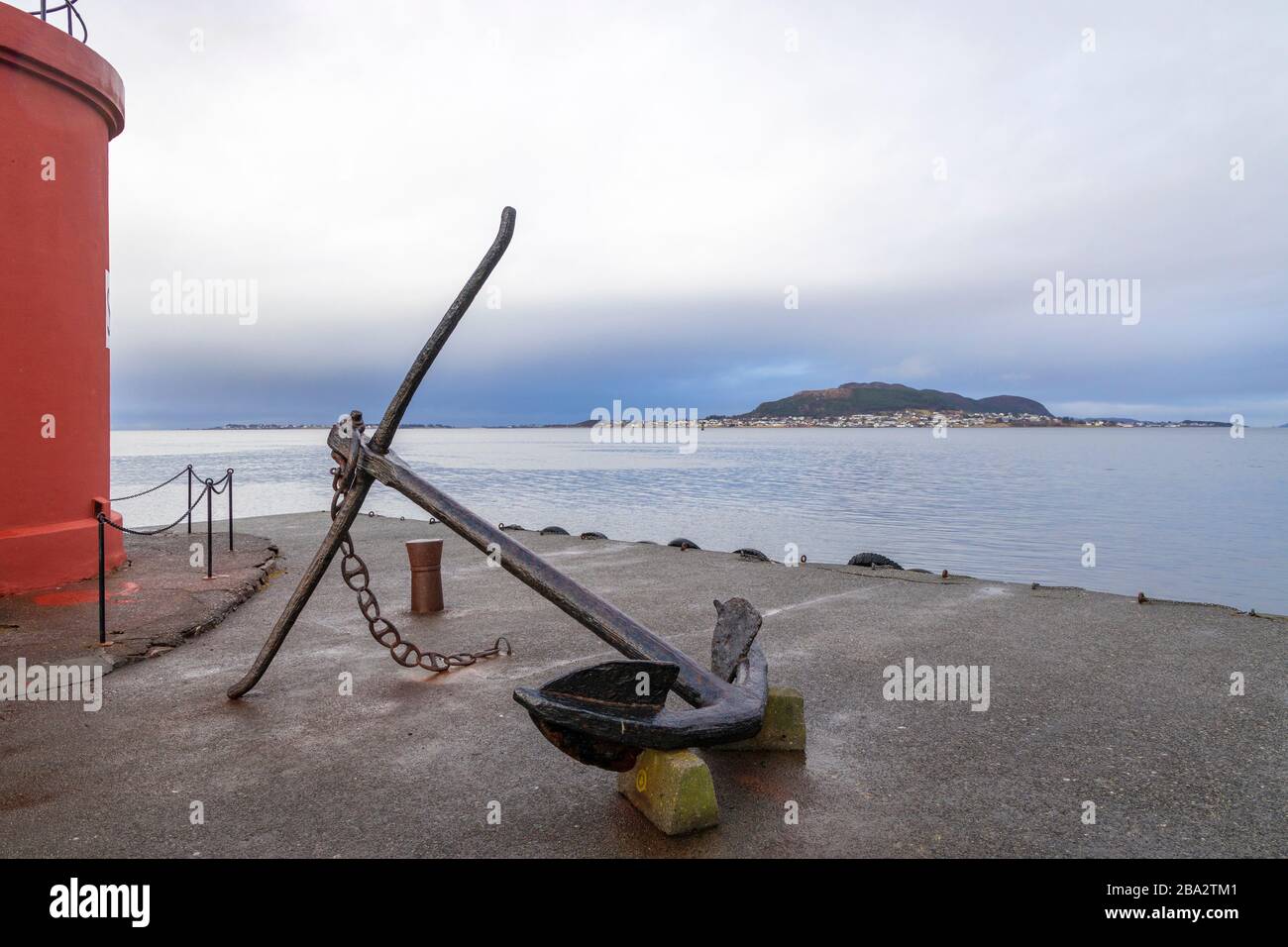 Red lighthouse and an old anchor at the port entrance of Alesund at the ...