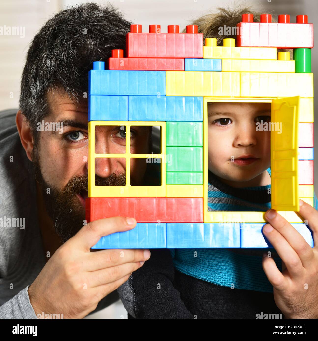 Father and son with calm faces behind colorful toy bricks construction ...