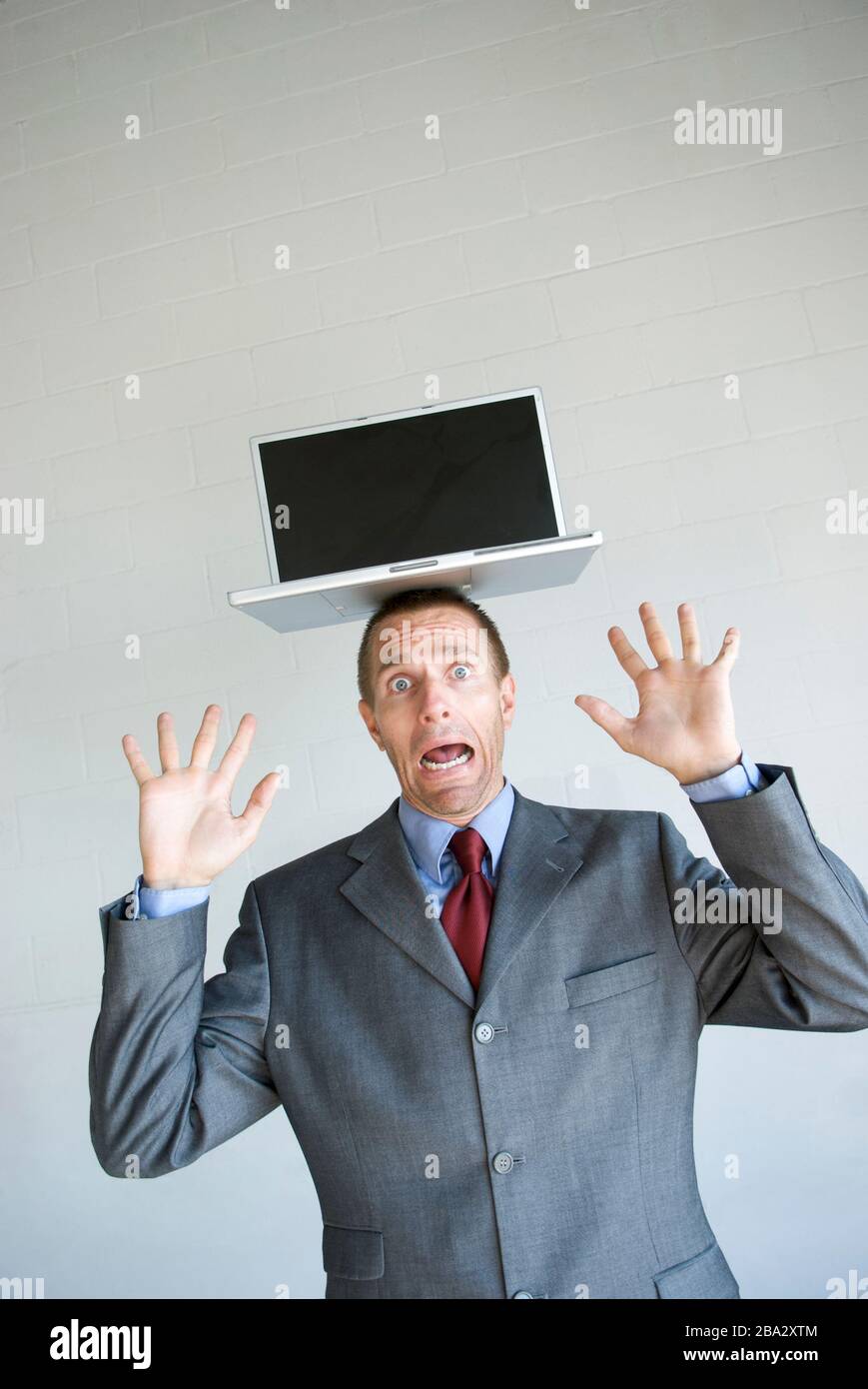 Businessman panicking while balancing a laptop computer with a blank ...