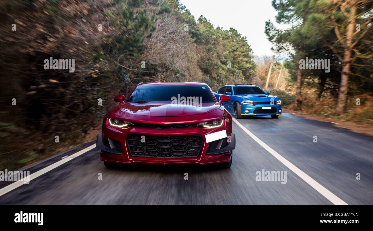 Red luxury business class sedan driving on the road. A blue car behind ...