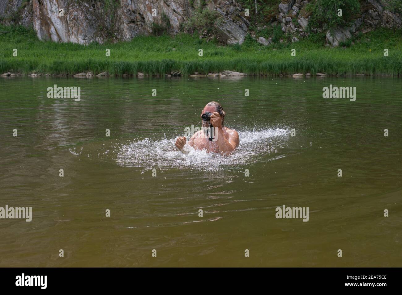 Mature caucasian man holding waterproof camera and swimming in river ...