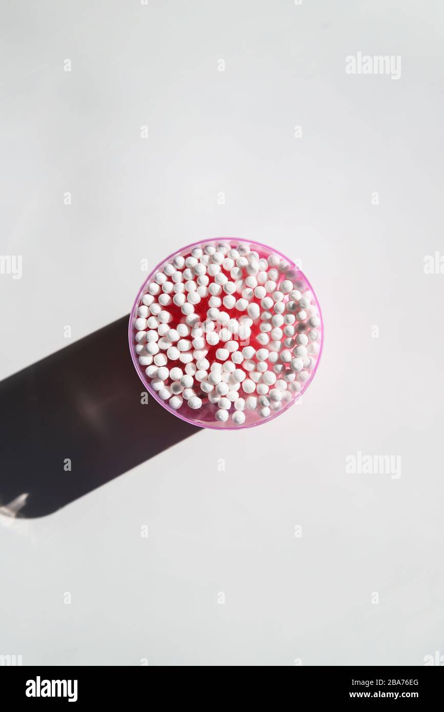 Pink cotton swab in plastic jar on white background with strong shadows ...
