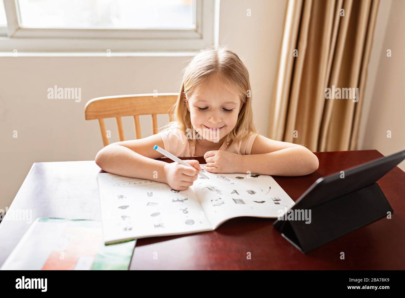 Pretty schoolgirl studying homework during her online lesson at home ...