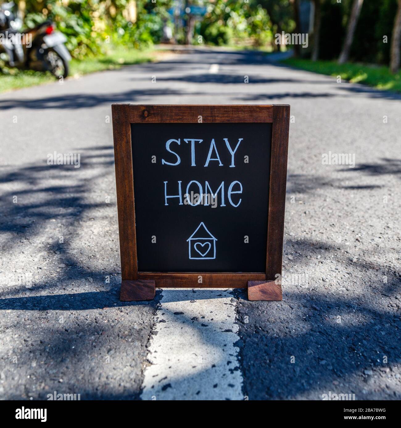 Black board sign STAY HOME standing in the empty street. Square image ...