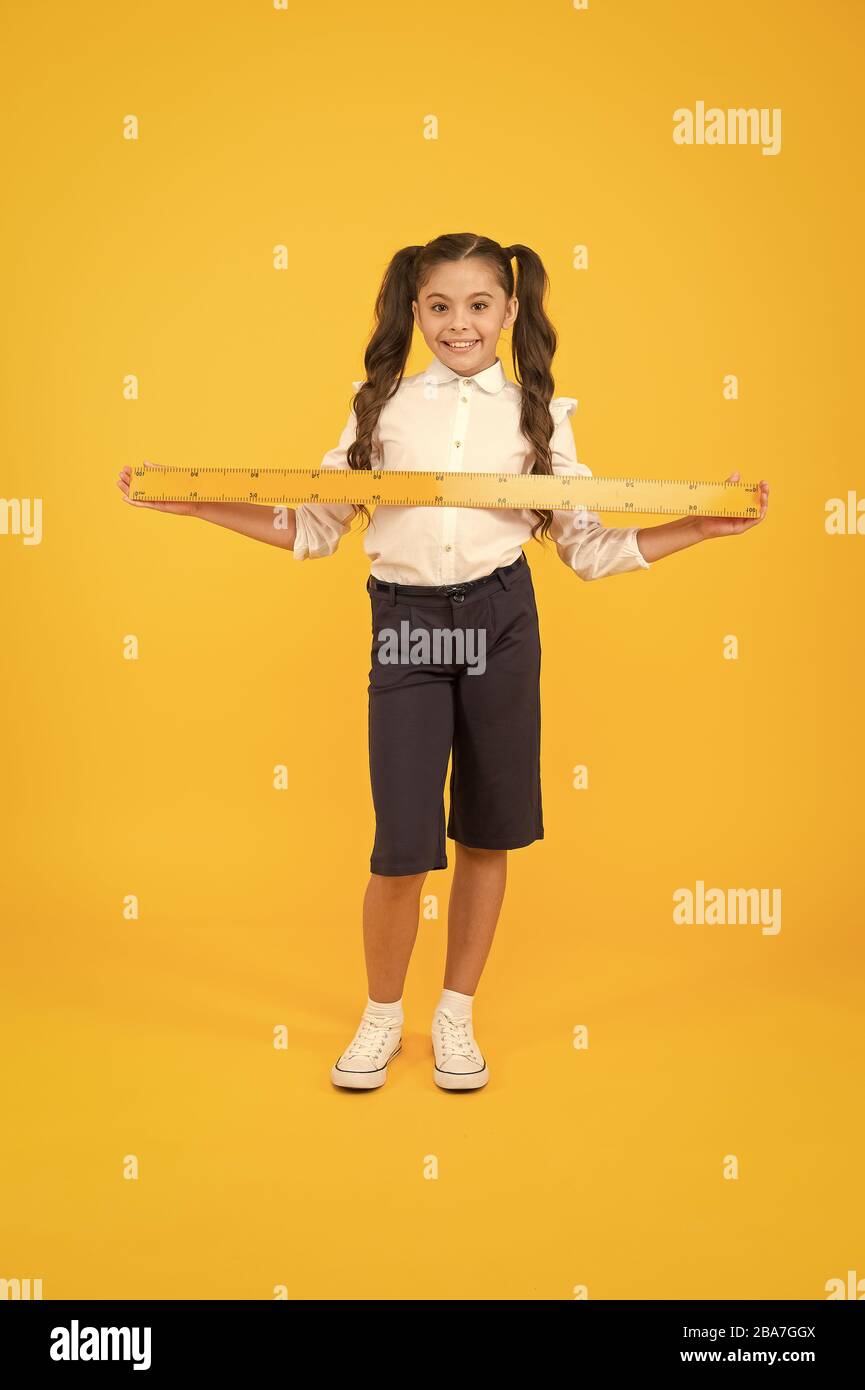 Measuring length. Little girl holding metric ruler on yellow background ...