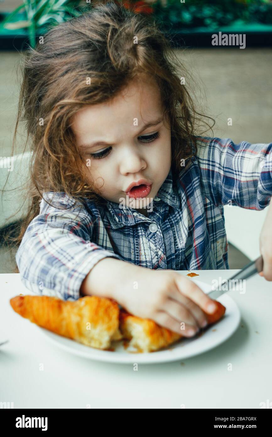 Cute little girl having breakfast with the croissant in a restaurant ...