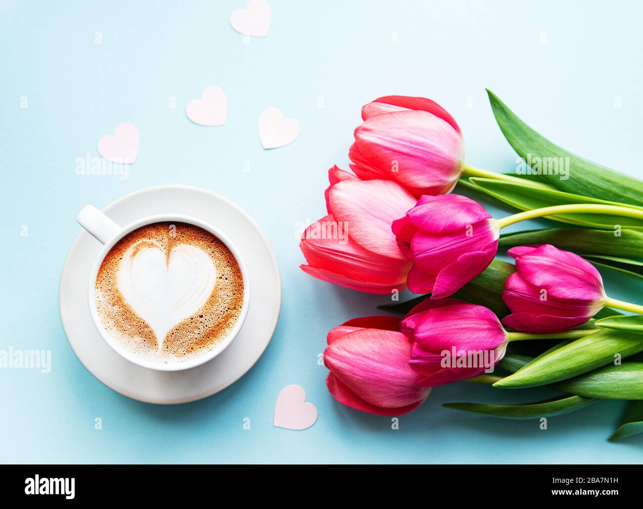 Coffee cup with latte art and pink tulips on the blue background. Top ...