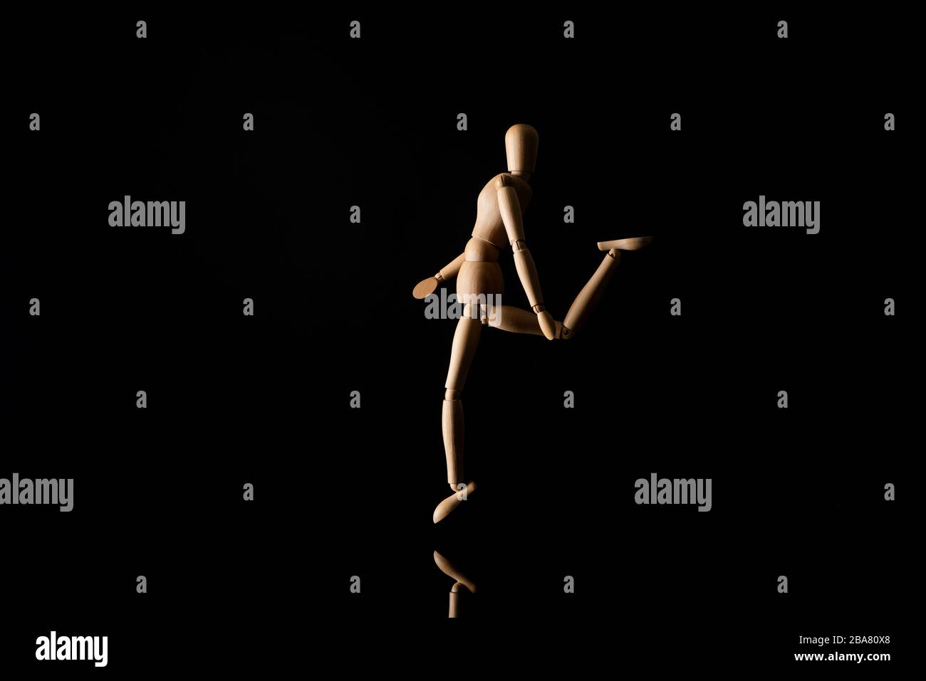Wooden doll imitating raising leg on black background Stock Photo - Alamy