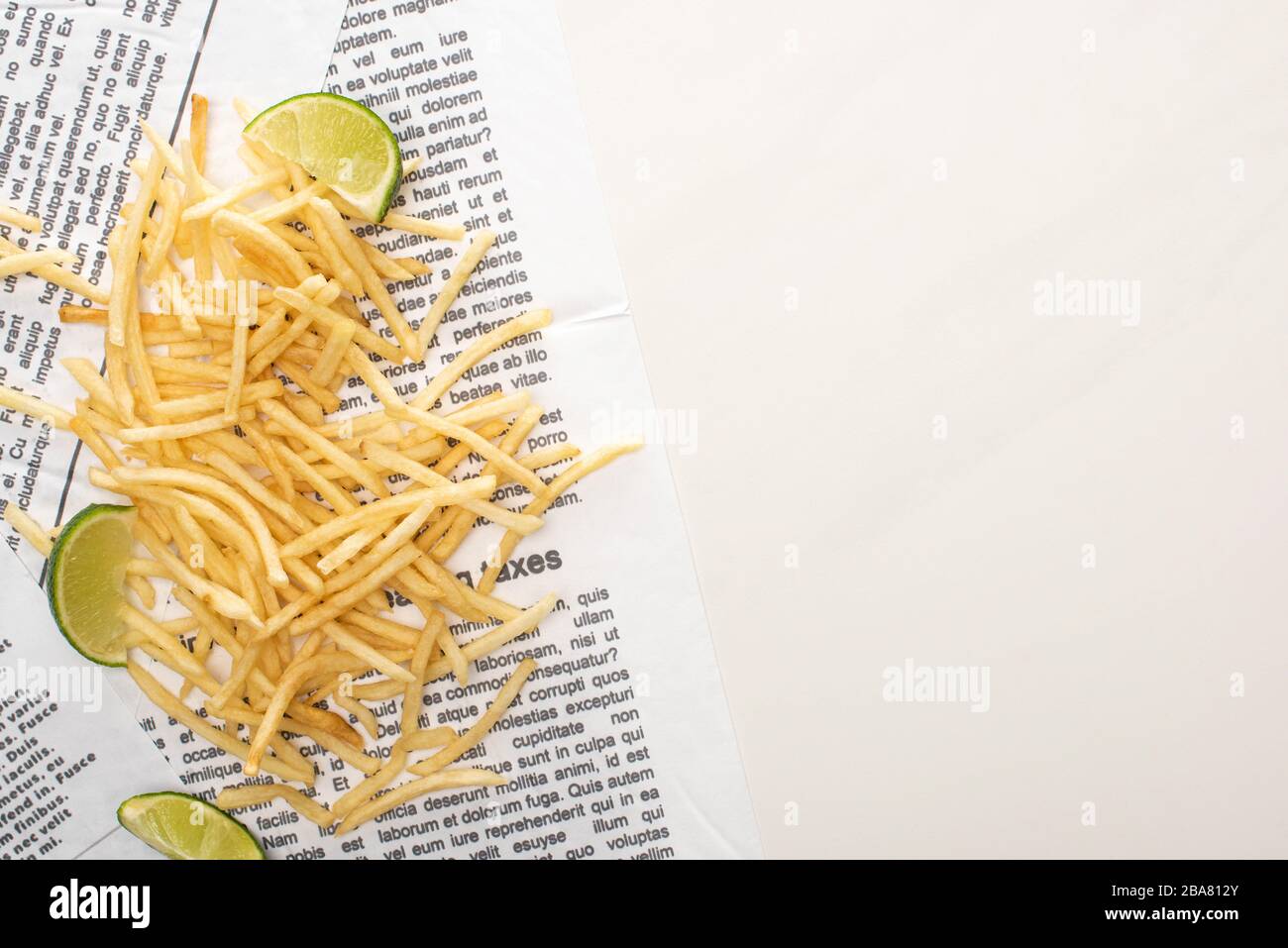 top view of crispy french fries and sliced lime on newspaper on white ...