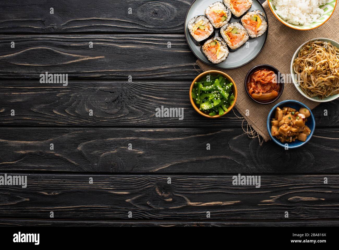 top view of bowls with tasty korean side dishes near gimbap on wooden ...