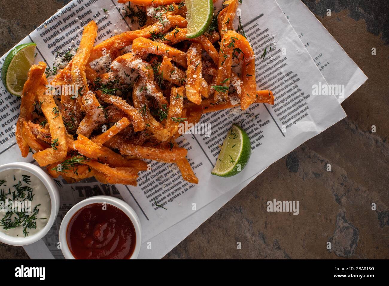 top view of tasty french fries and sliced lime on newspaper and marble ...