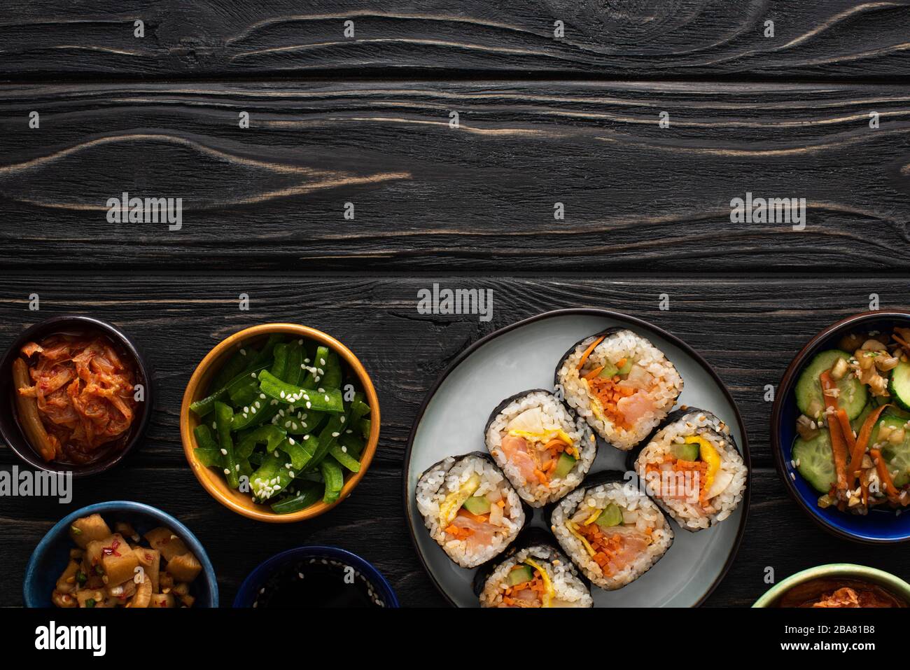 top view of plate with korean gimbap near side dishes on wooden surface ...