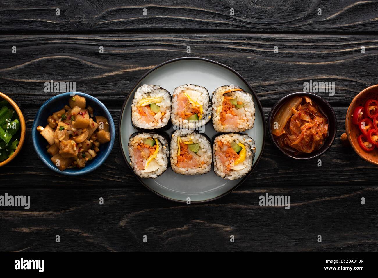 top view of plate with gimbap near side dishes in bowls on wooden ...