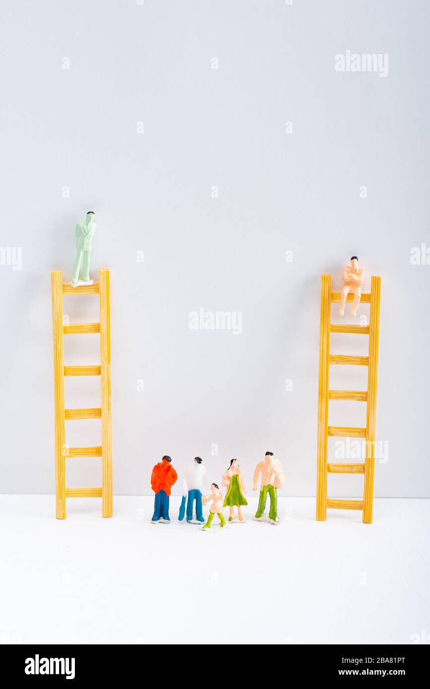 Plastic people figures near dolls on ladders on white surface on grey ...