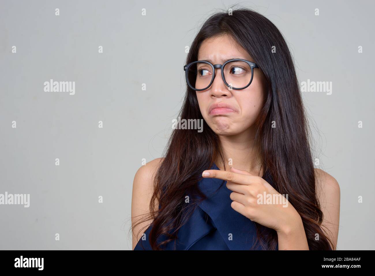 Face of stressed young Asian businesswoman pointing to side and looking ...