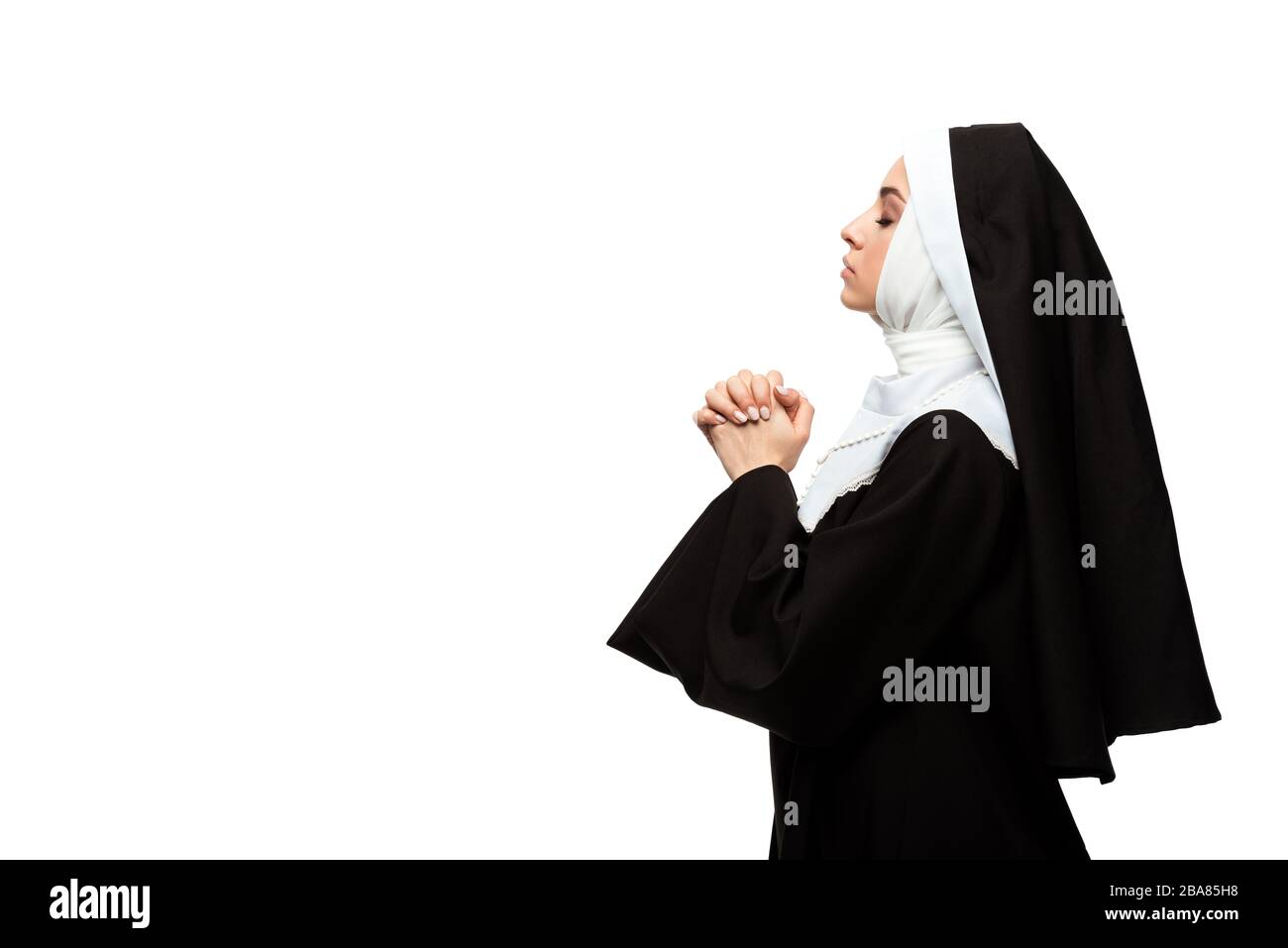 attractive nun praying with closed eyes and hands together isolated on ...