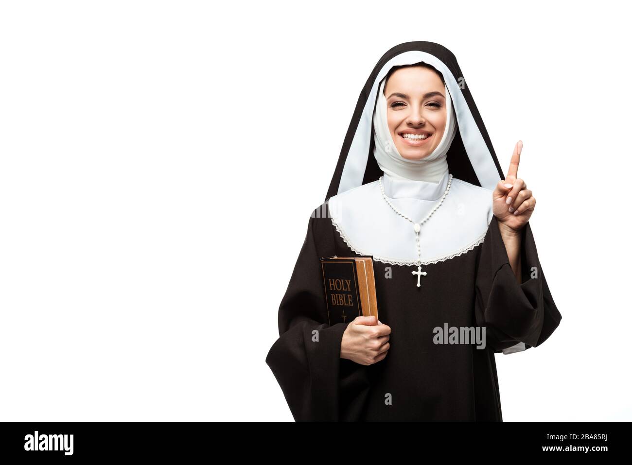 cheerful nun holding bible and pointing up with idea isolated on white ...